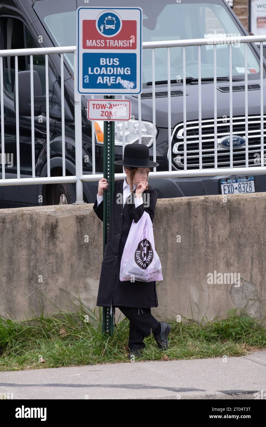 An orthodox Jewish boy with long peyus waits for a bus on Forest Road ...
