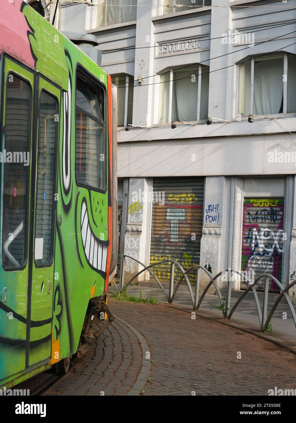 Graffiti painted tram on motion on rails taking a curve along building ...