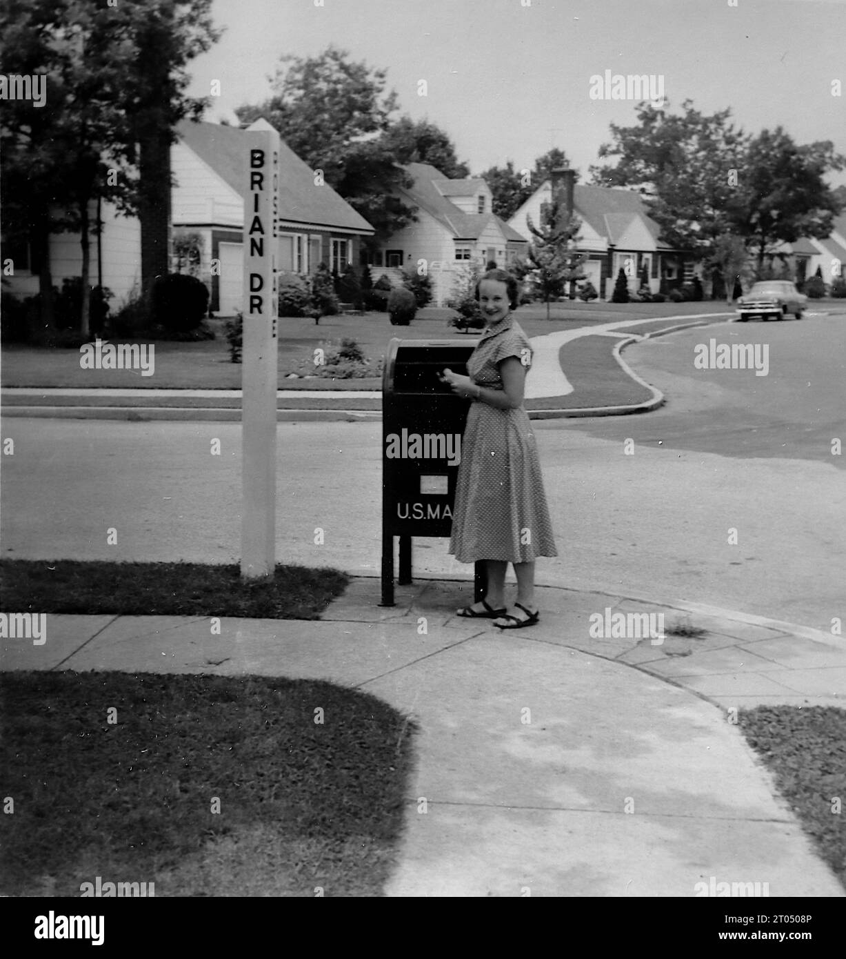 A lady standing beside a US Mailbox and a road sign for Brian Drive in ...
