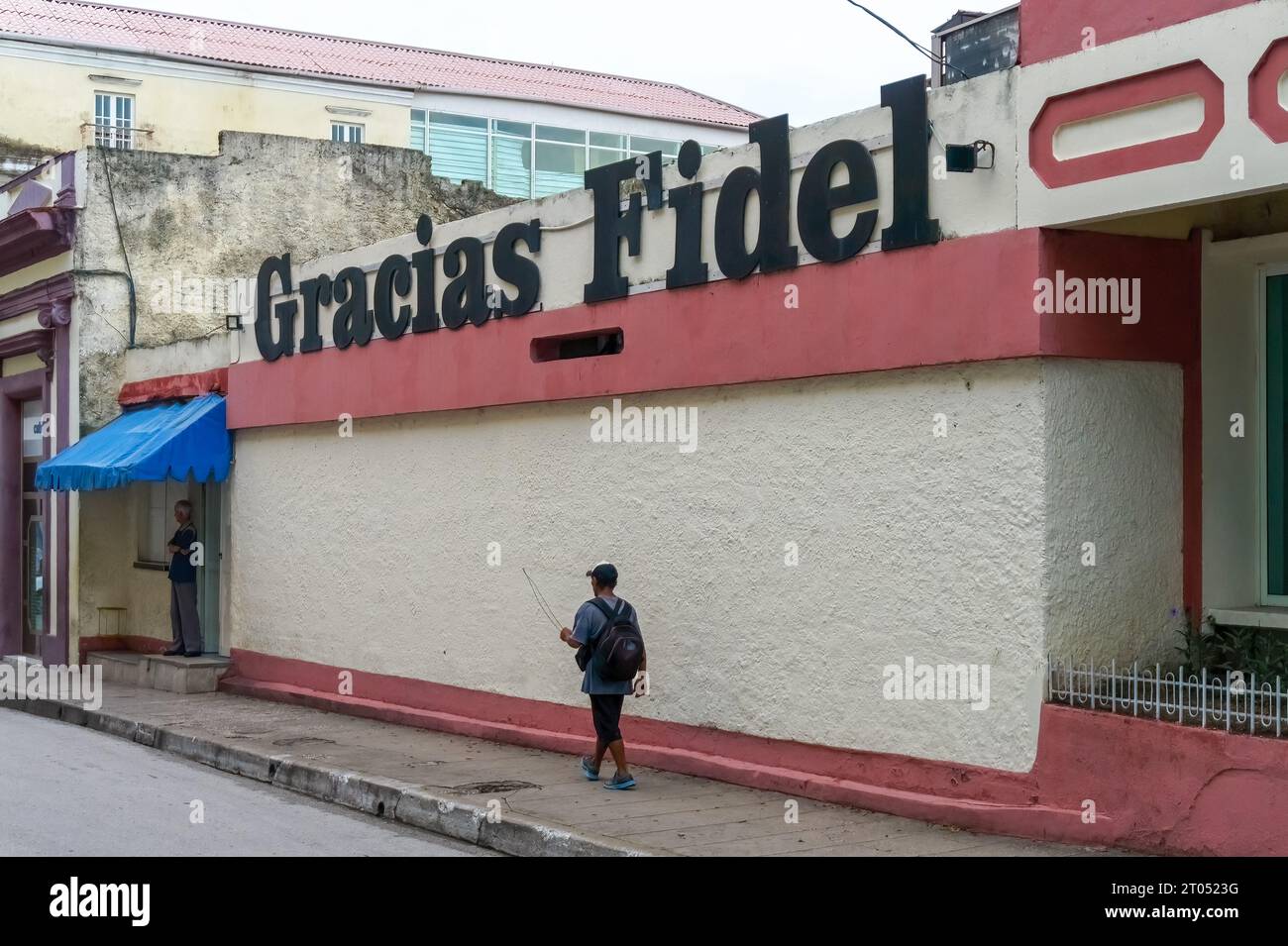 A Cuban man walks by a sign with text in Spanish language. It reads ...