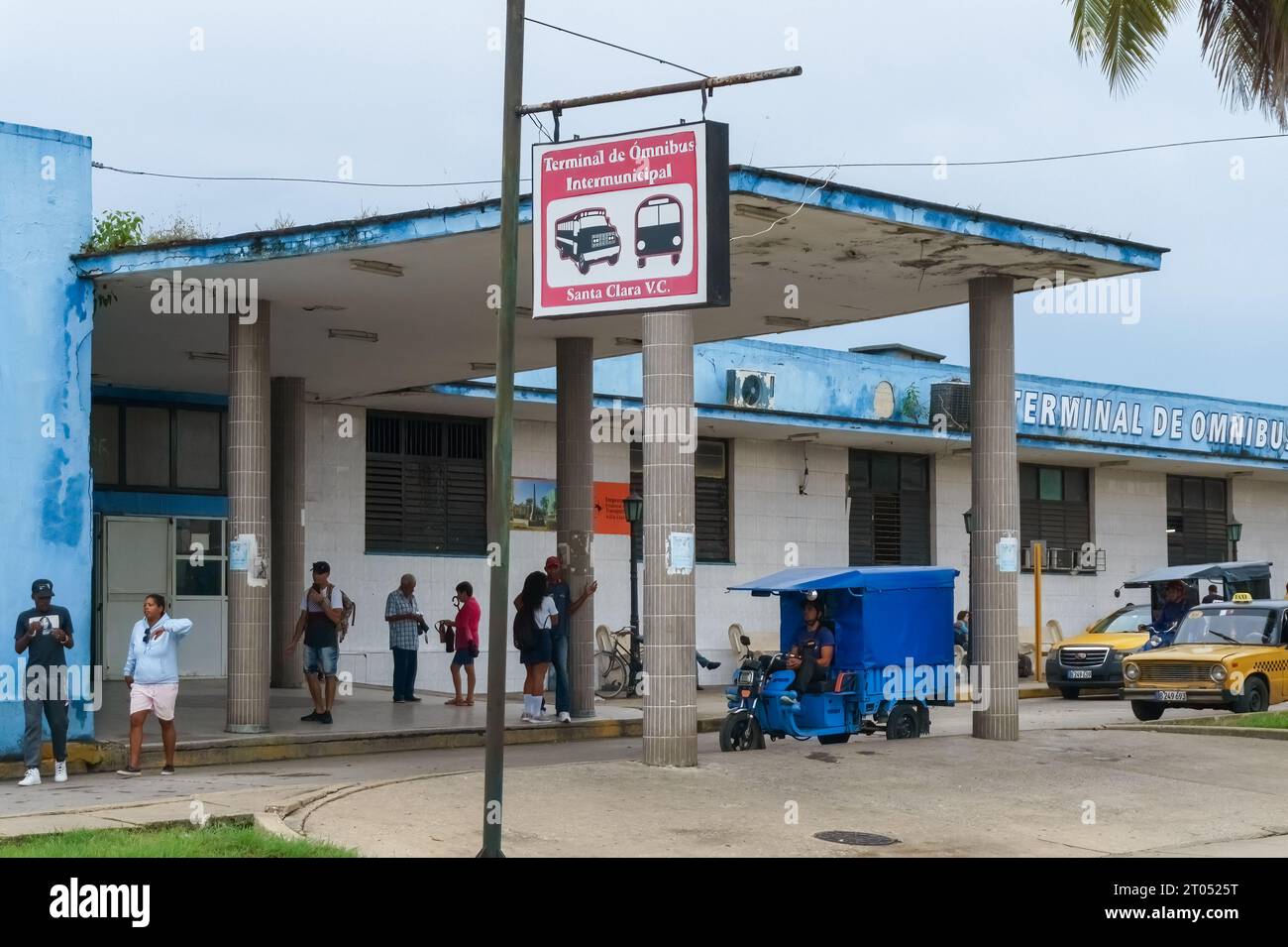 Cuban people walk by an electric tricycle and taxis outside the ...