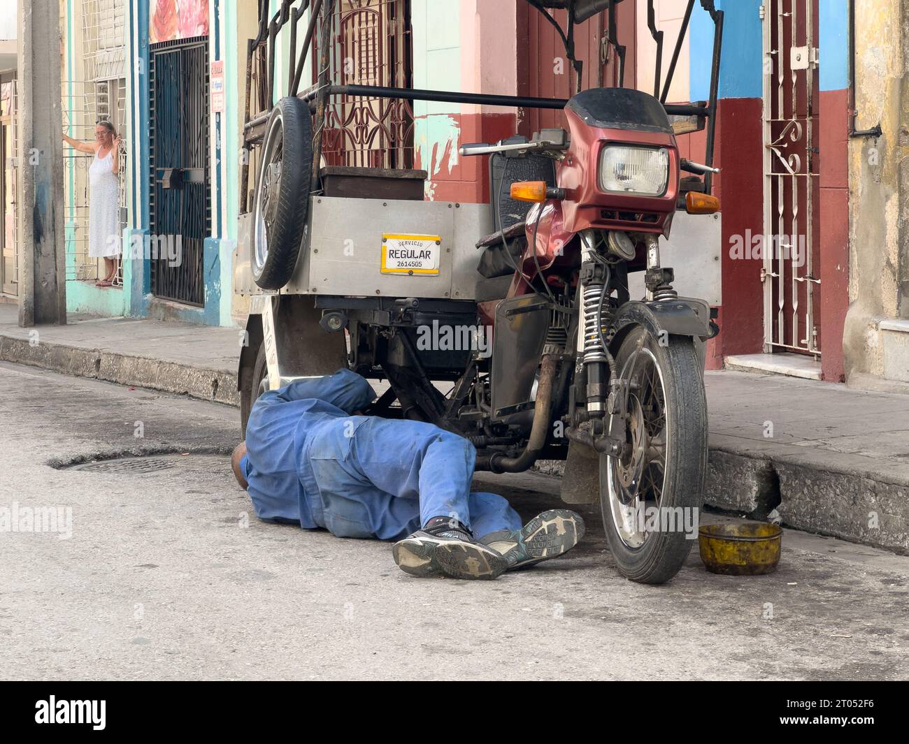 A Cuban man lays on the floor of a city street. He is traying to repair ...