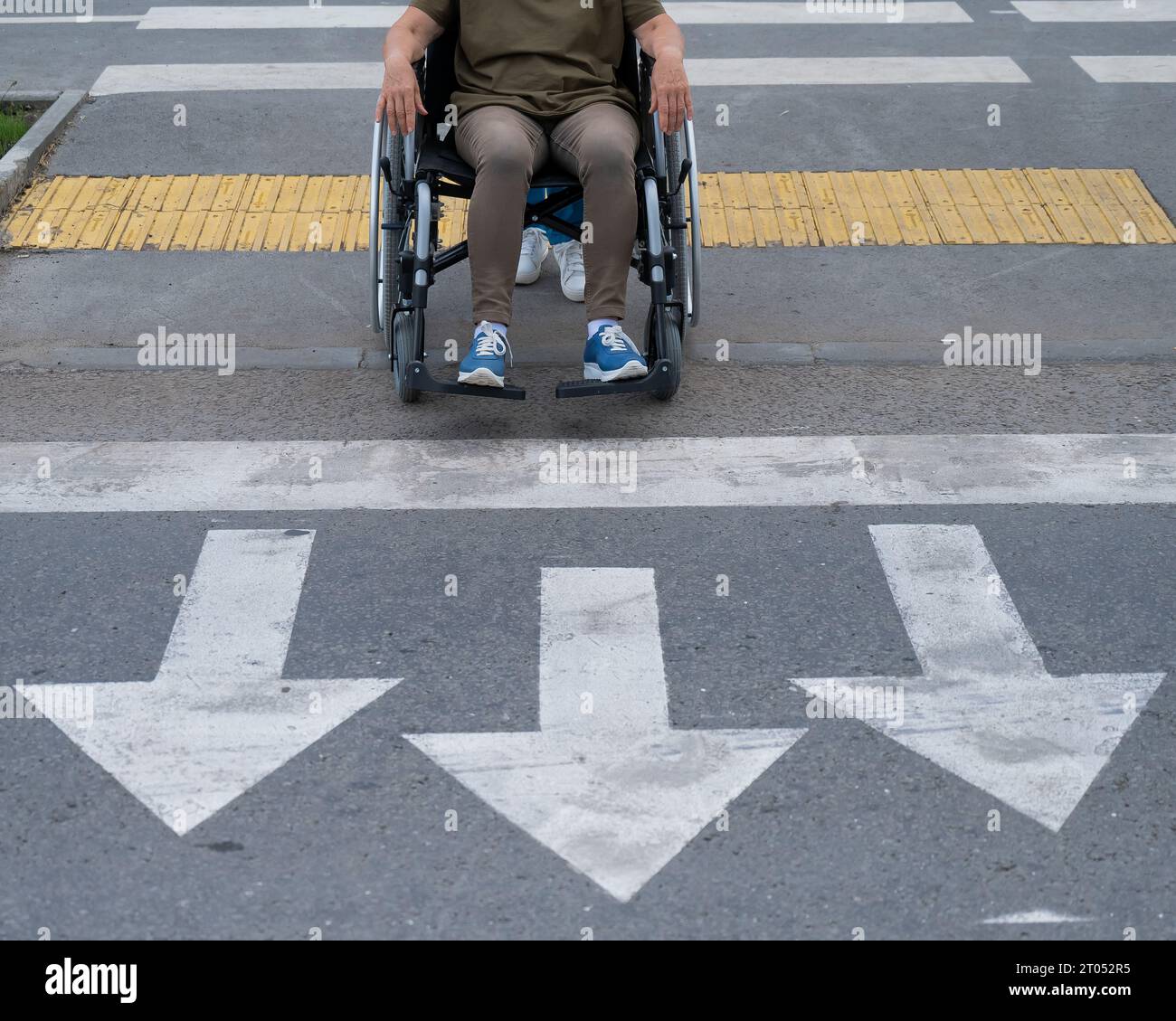 An elderly woman in a wheelchair is about to cross the road at a ...