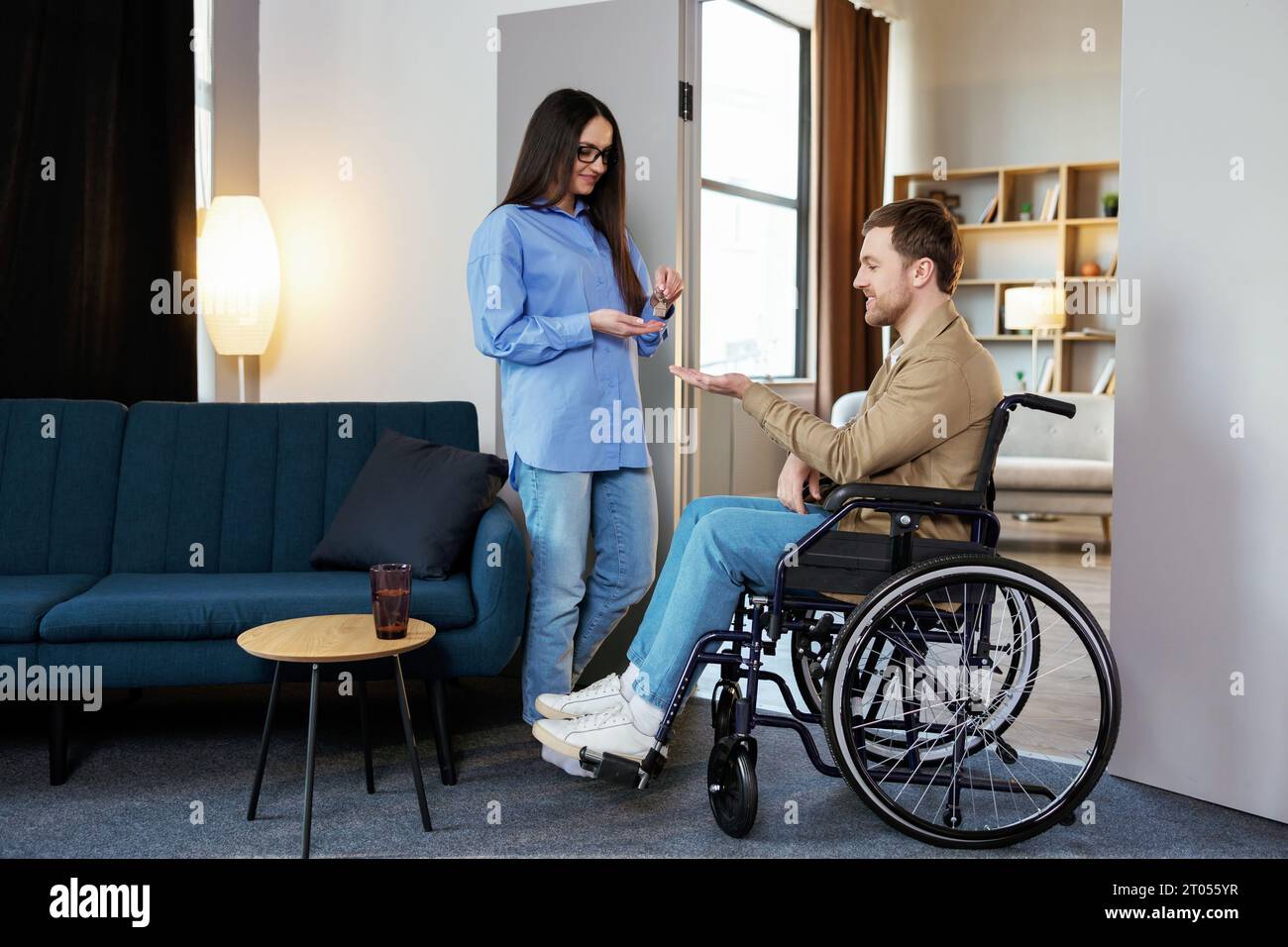 Man in wheelchair extend her hand palm up to side. Woman giving key ...
