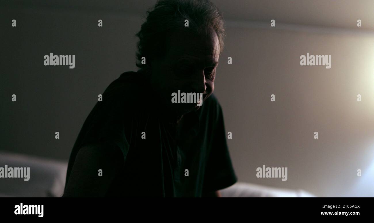 Worried senior man sitting by the side of the bed in the night unable ...