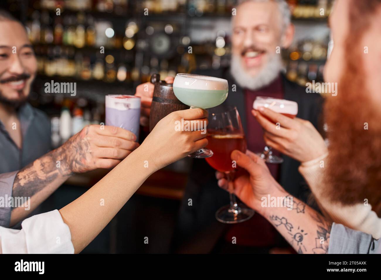 joyful multiethnic workmates clinking glasses with cocktails in bar ...