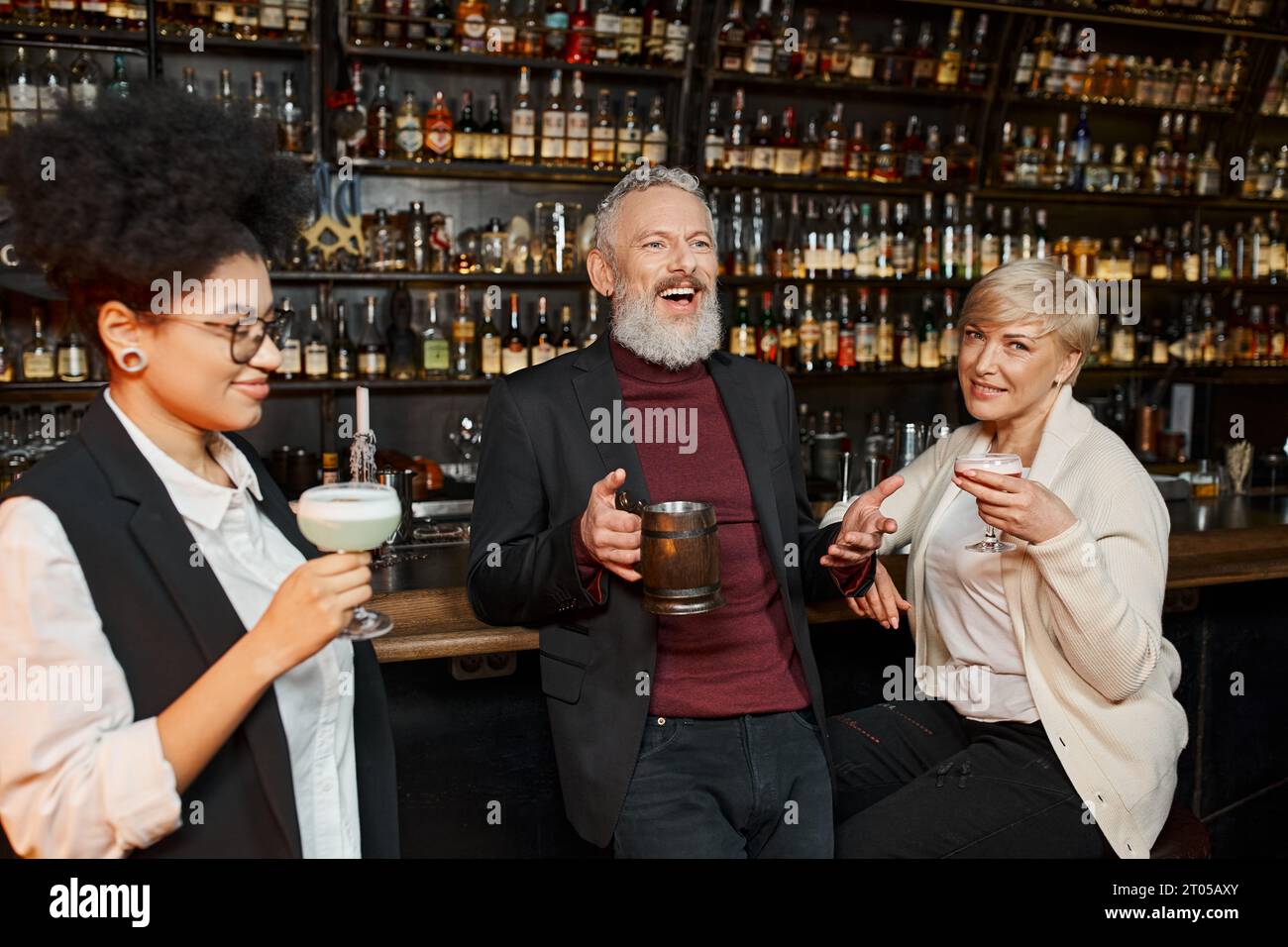cheerful bearded man laughing near multiethnic women with cocktail ...