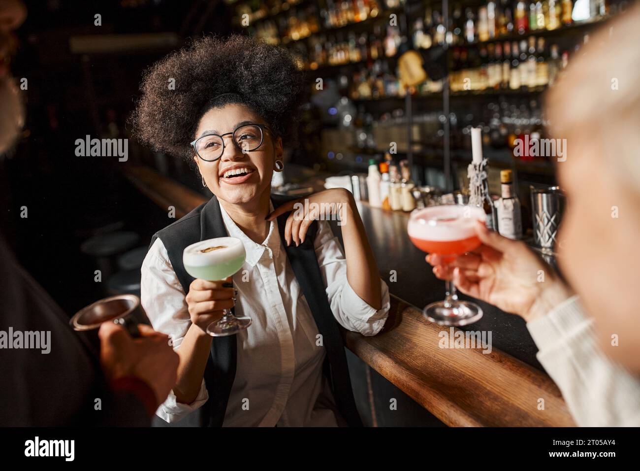 cheerful african american woman holding cocktail glass while spending ...