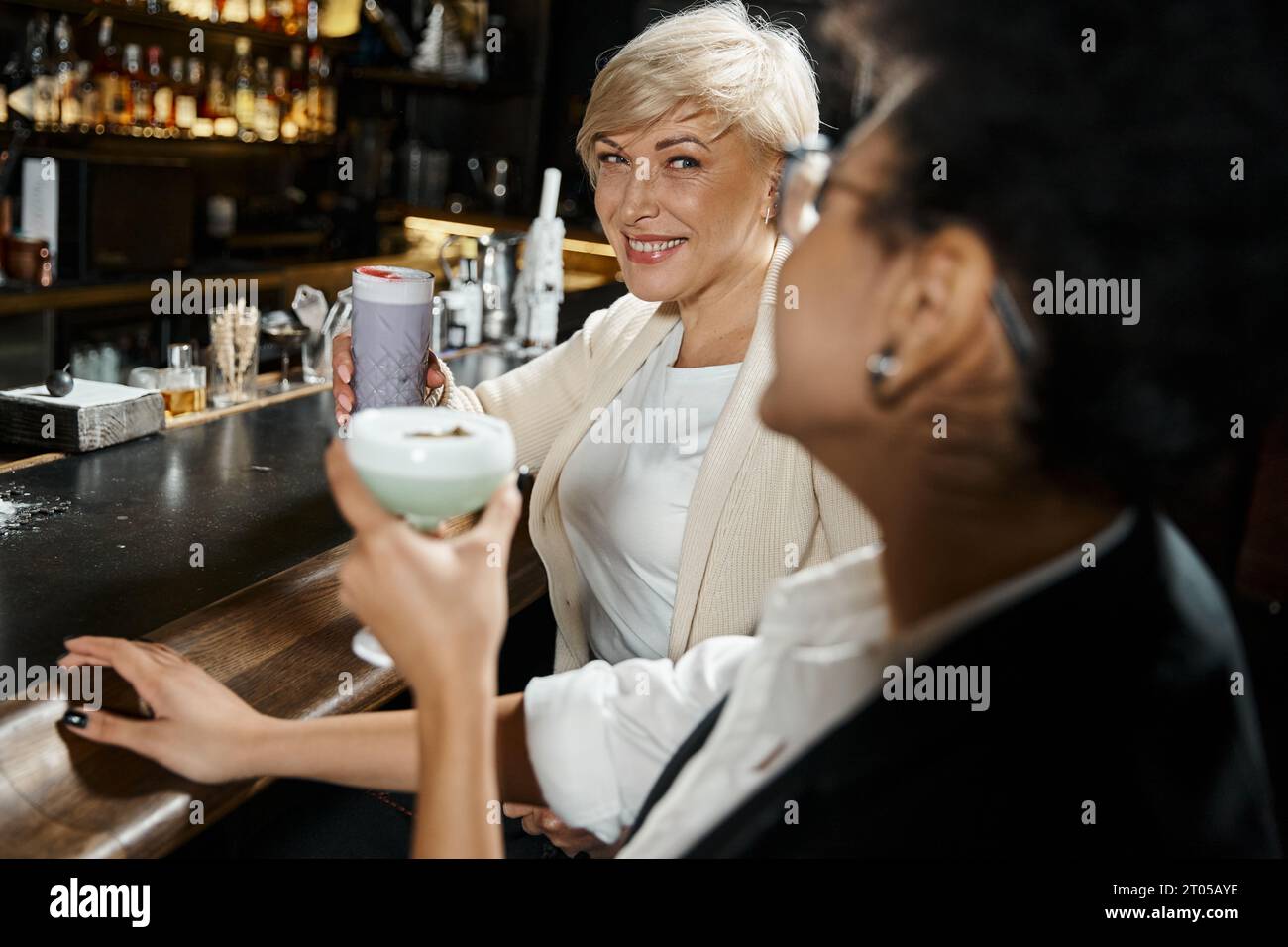 happy middle aged woman with female african american colleague drinking ...
