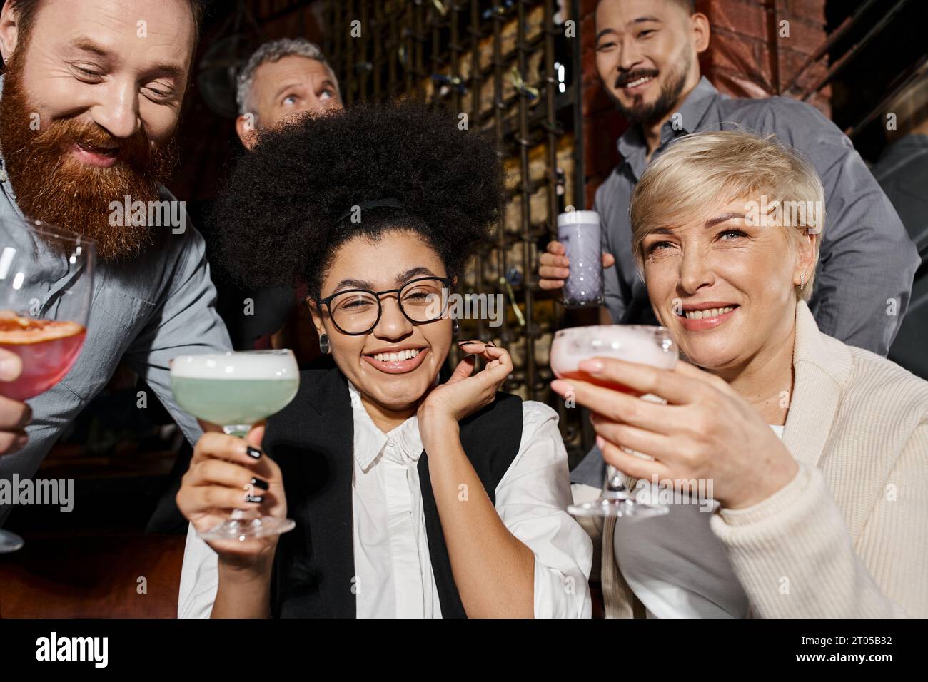 happy women with cocktails near bearded men in bar, multiethnic ...