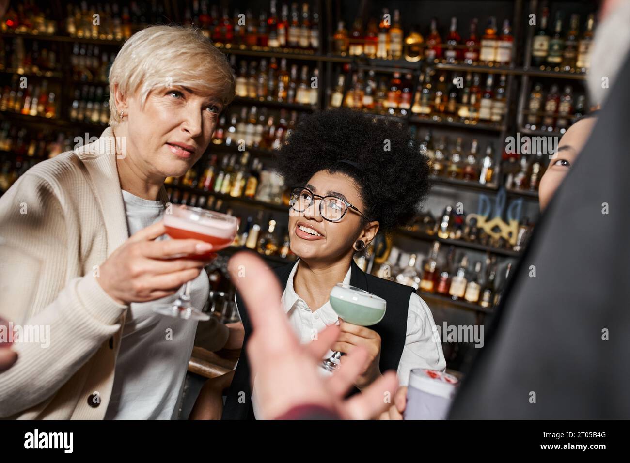 middle aged woman with cocktail glass talking to multicultural ...
