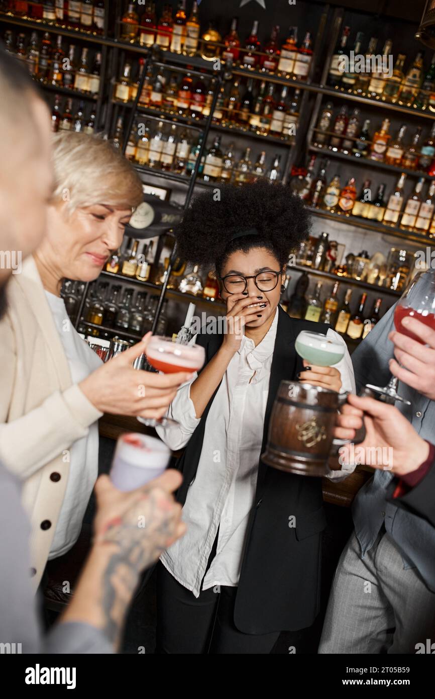 excited african american woman laughing with closed eyes near team of ...