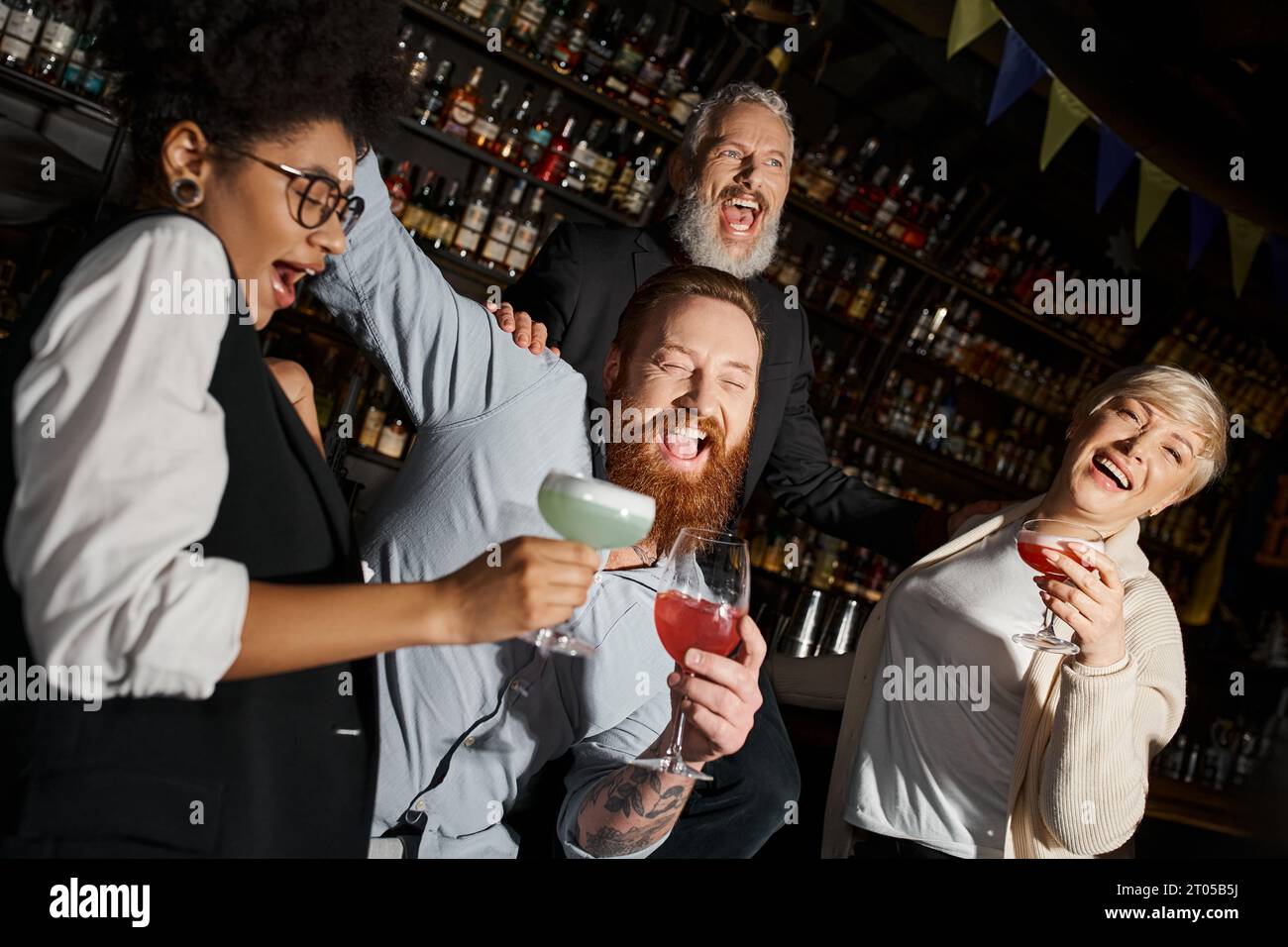 overjoyed multiethnic colleagues with cocktails laughing in bar ...