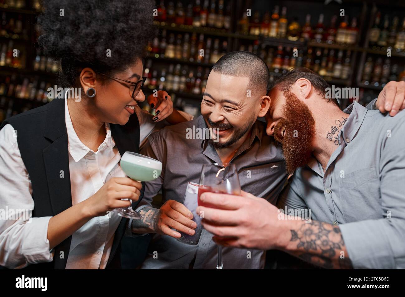 overjoyed multiethnic workmates with cocktails embracing and laughing ...