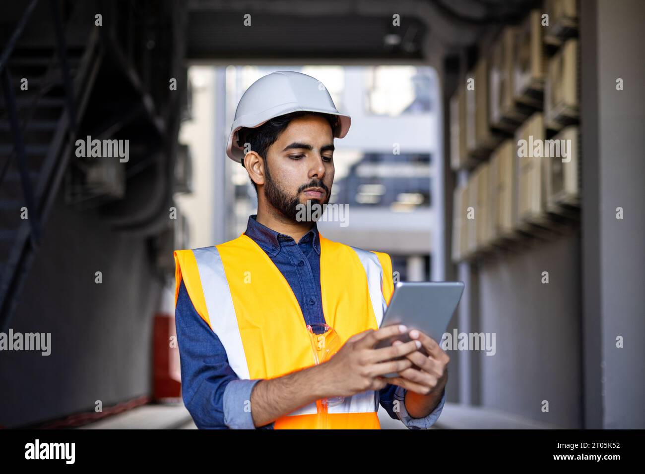 Serious thinking and focused engineer working in factory in hard hat ...