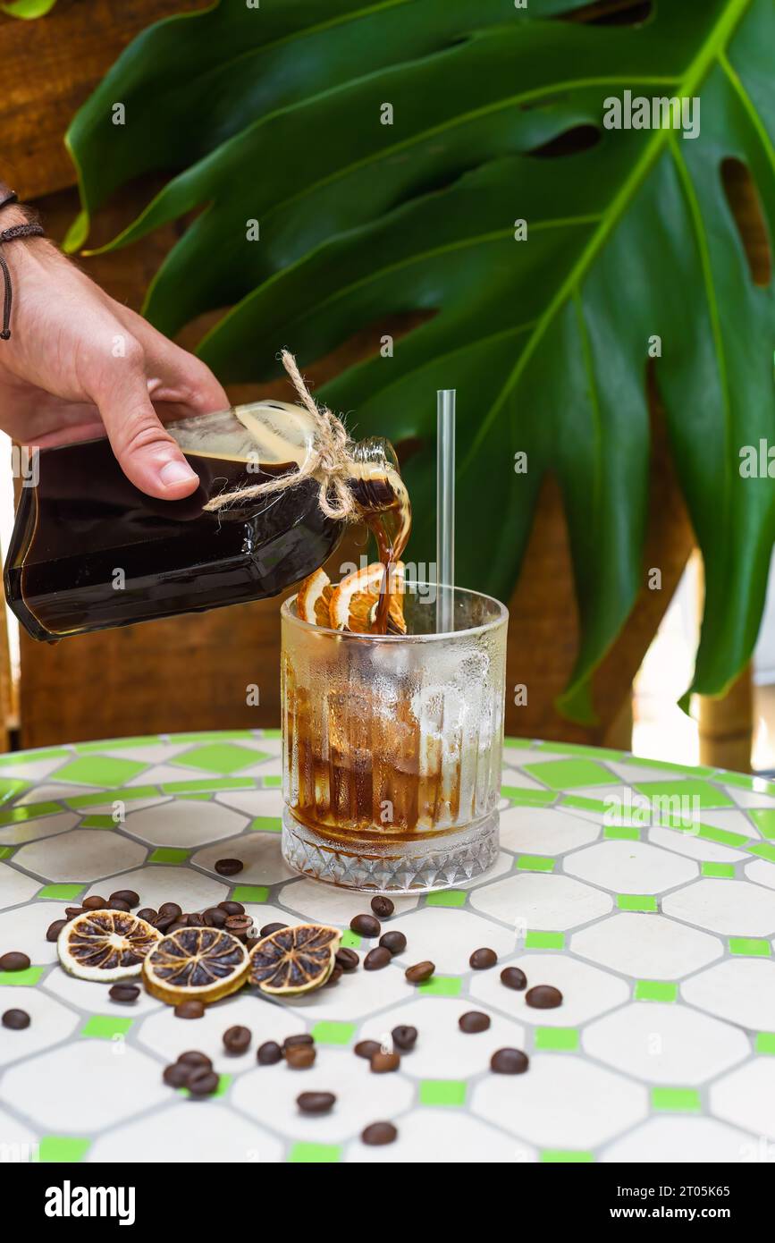 Hand pouring cold brew coffee in a bottle with transparent glass full ...