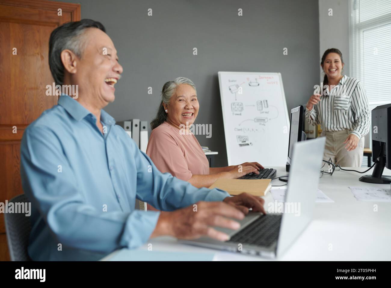 Senior couple having fun in computer class, they are typing and joking ...