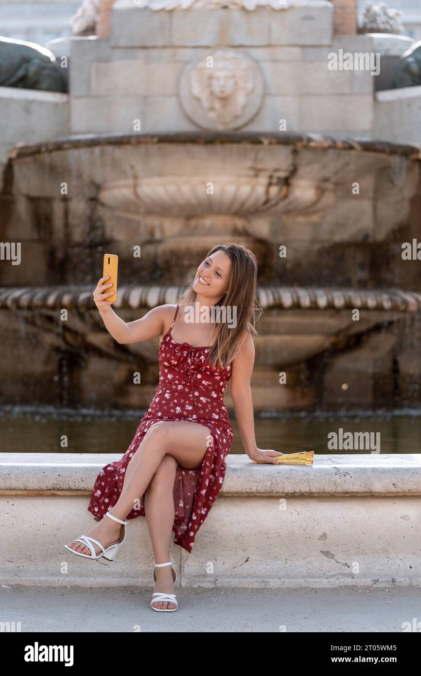 Woman in dress and heels smiling while taking a selfie with her cell ...