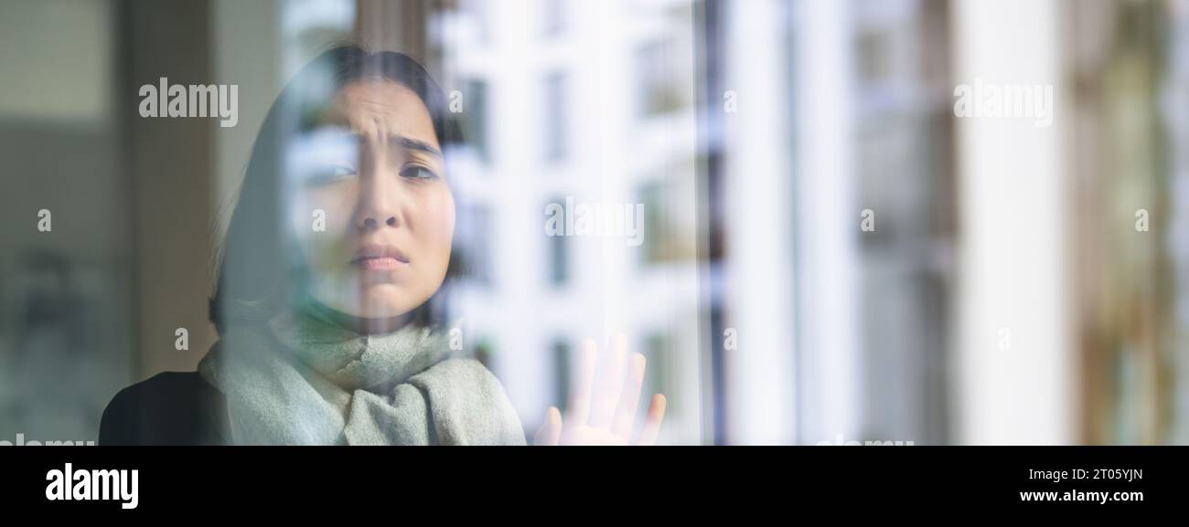Asian woman feels unwell, stays at home, looks outside window with ...