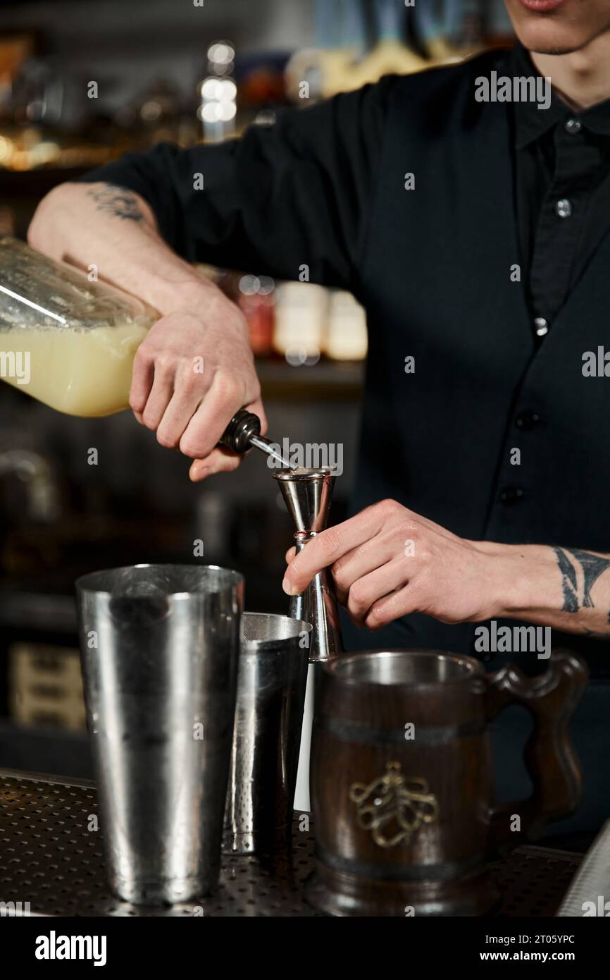 cropped view of bartended pouring alcohol drink into jigger while preparing cocktail on bar ...
