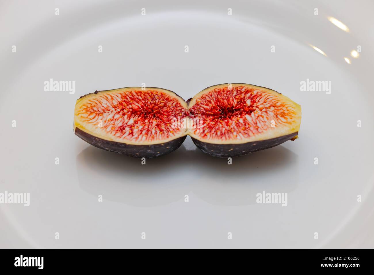 Two halves of a ripe sliced fig on a white plate photographed in studio ...