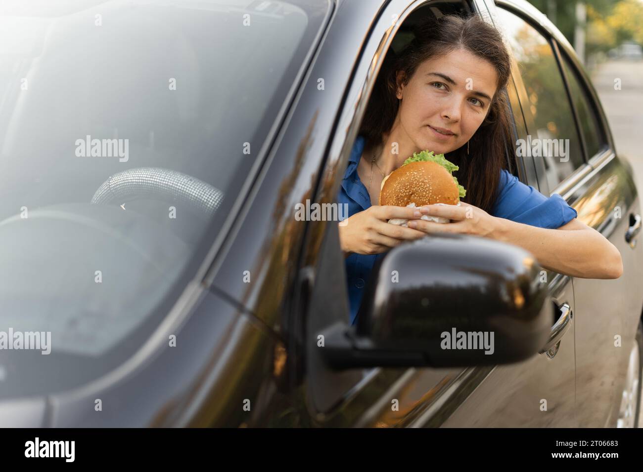 Female driver eating a delicious fatty hamburger in her car while ...