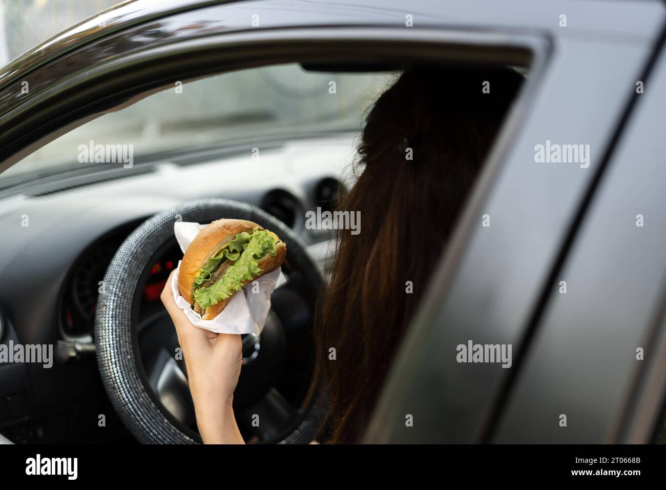 Woman driving car while eating delicious hamburger. Standing in traffic ...