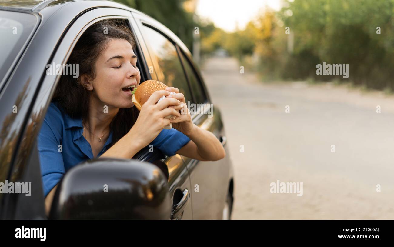 Beautiful woman eating a burger while driving, unhealthy lifestyle ...