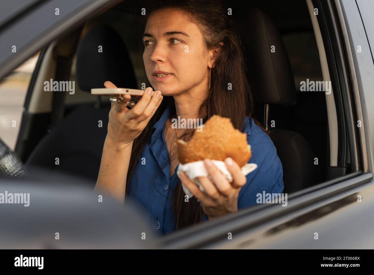 Close-up of woman using mobile phone, eating burger and talking on the ...