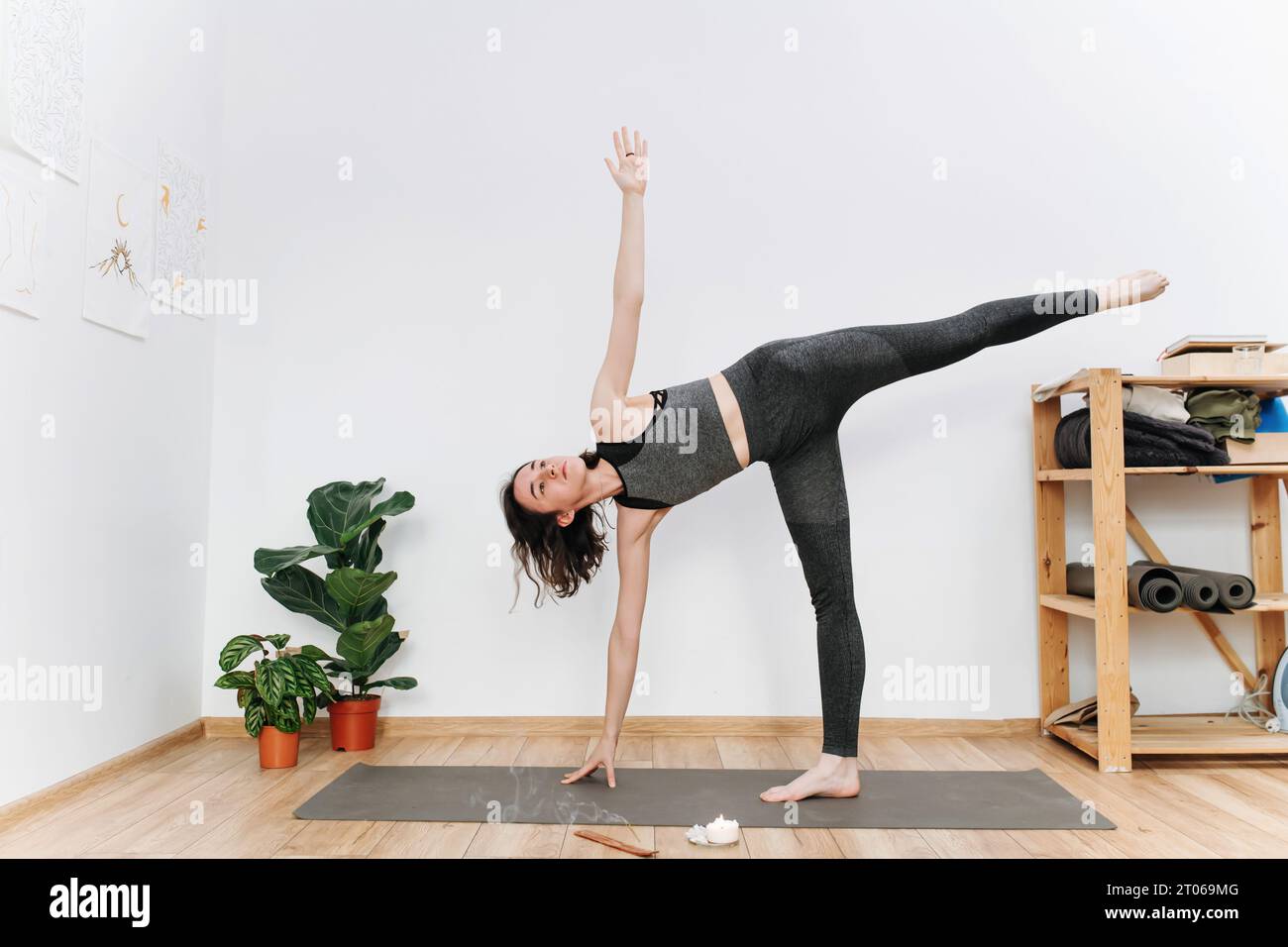 Doing yoga exercises, a girl stands on one arm and one leg, keeping her ...