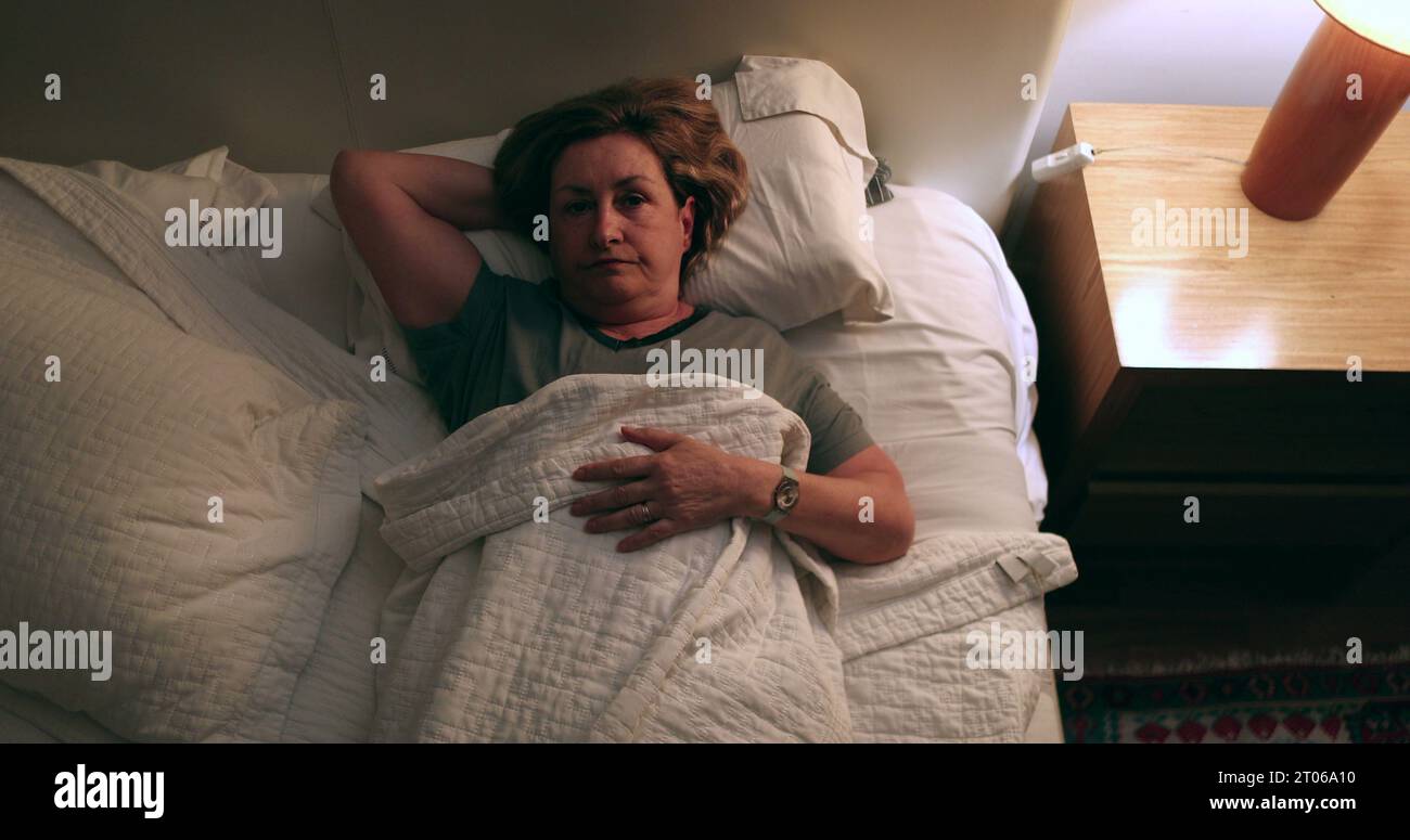 Pensive older woman lying down in bed, turns off nightstand light off and goes to sleep Stock ...