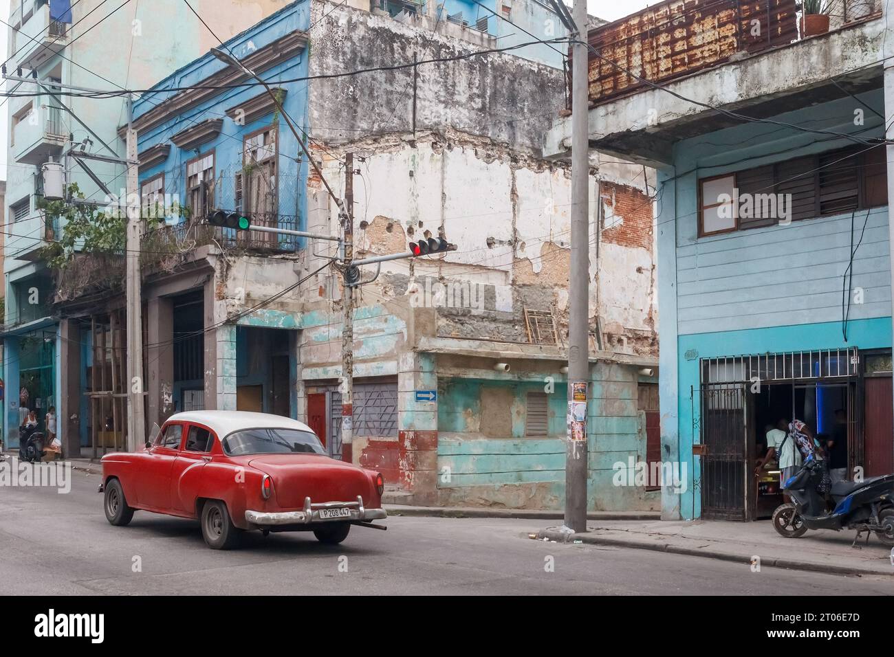 A vintage red American car drives in a city street by a run down ...