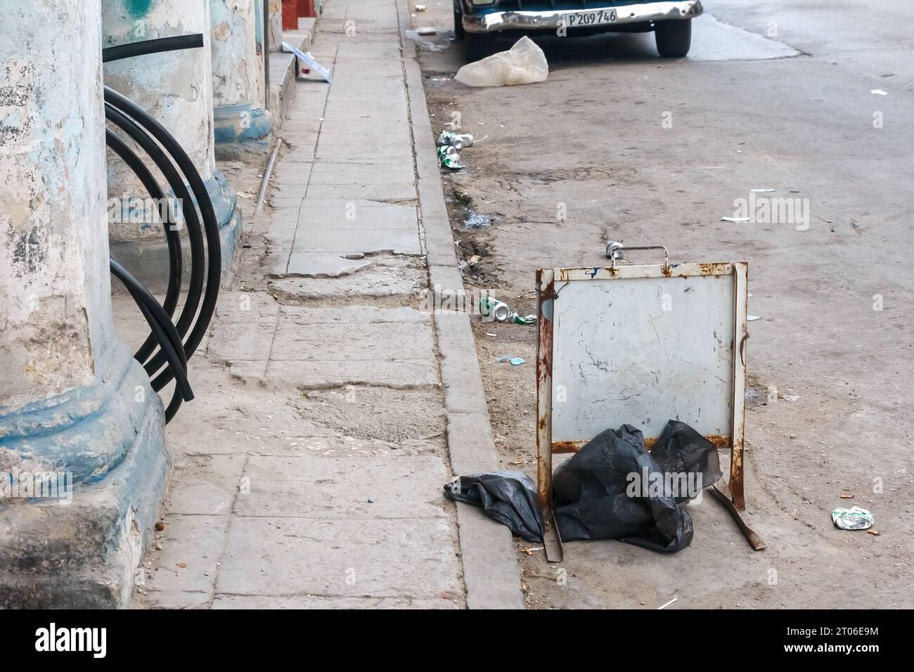 Broken and dirty sidewalk with garbage in the street curb. There is a ...