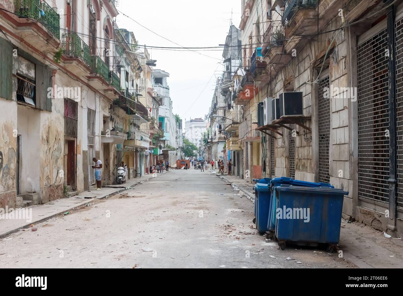 A dirty city street with weathered building facades. Two garbage bins ...
