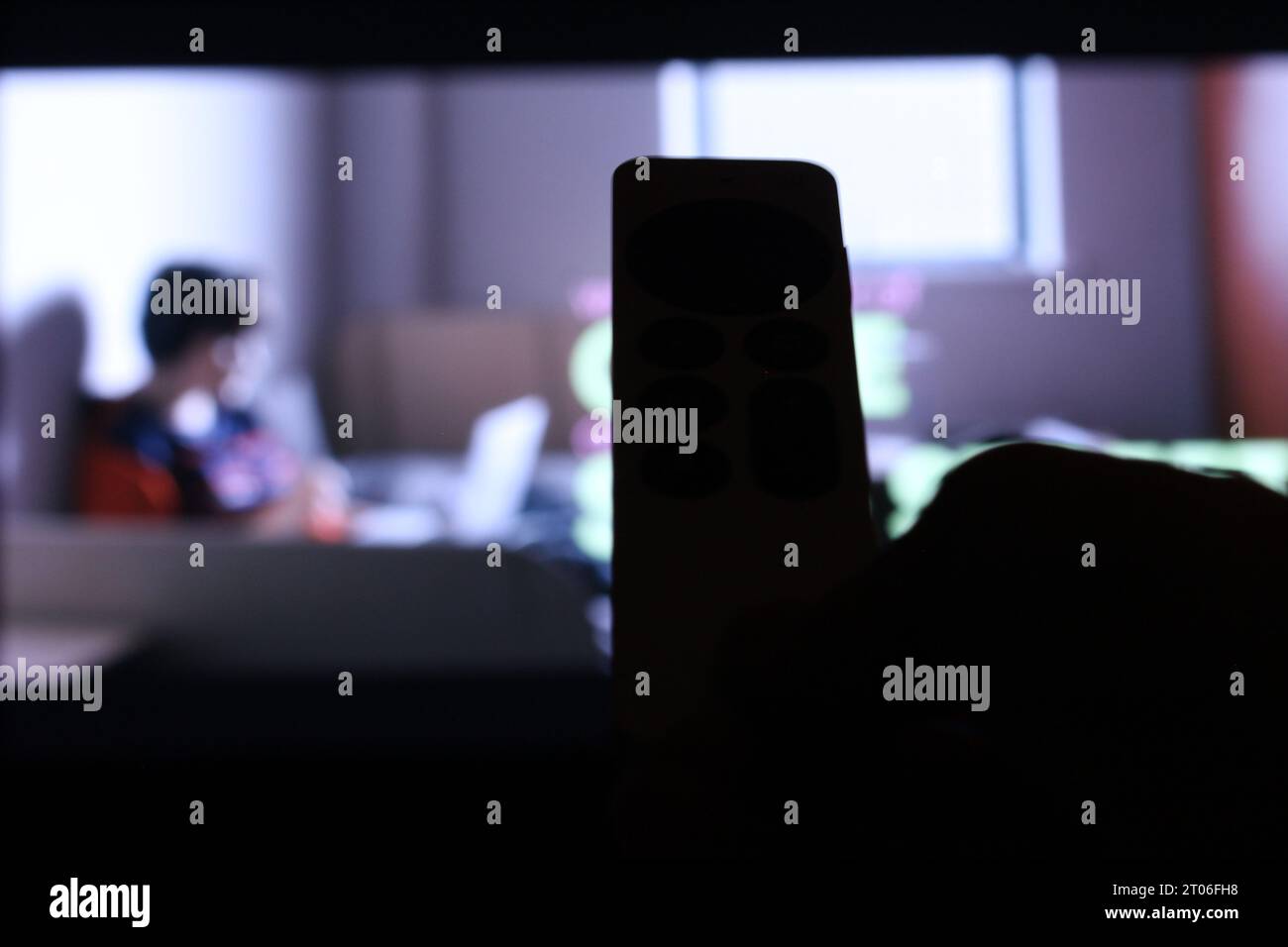 Shadow of a tv remote in front of a blurry tv screen playing a film ...