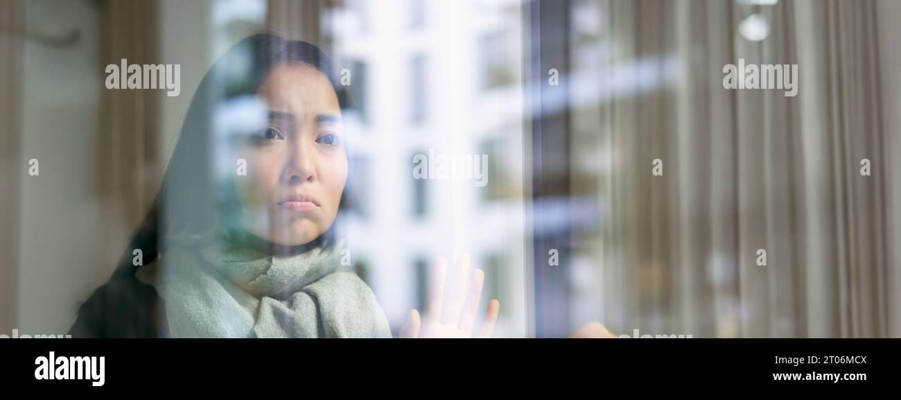 Asian woman feels unwell, stays at home, looks outside window with ...