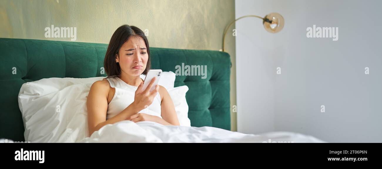 Portrait of concerned asian woman holding mobile phone, receive bad ...