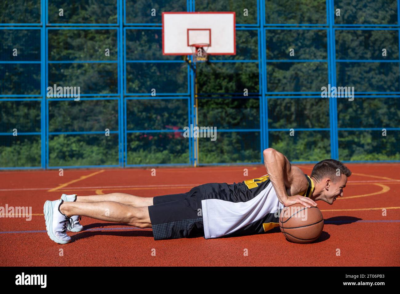 Athletic young man doing push ups with a basketball ball on basketball ...
