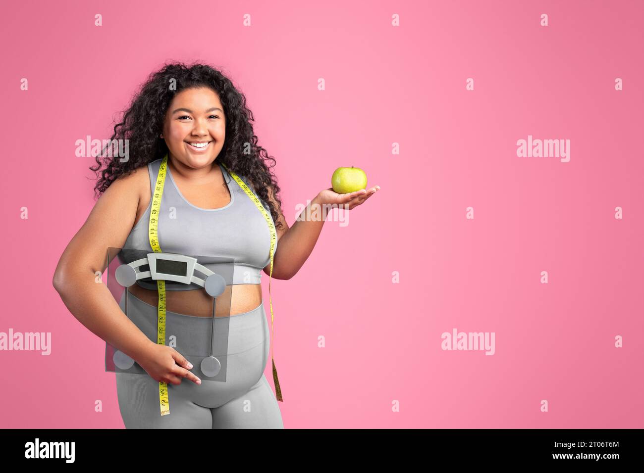 Glad black body positive woman in sportswear holding apple and scales ...