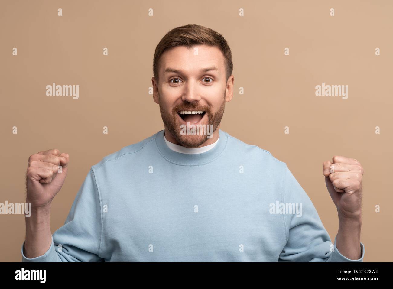 Happy cheerful man shows win victory gesture on beige background ...