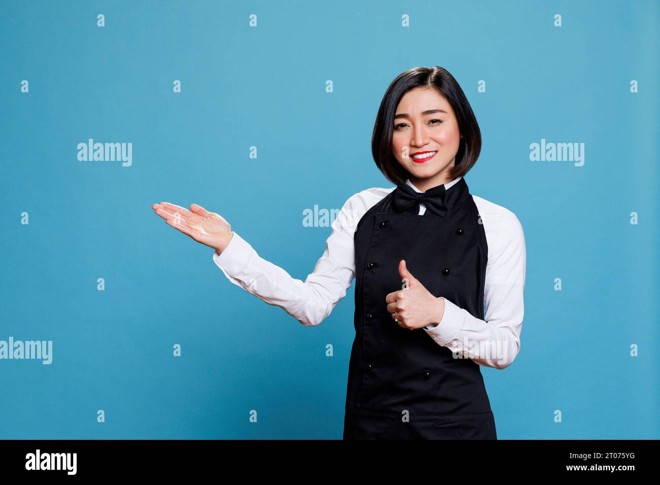 Cheerful asian woman receptionist showing thumb up and pointing to side ...