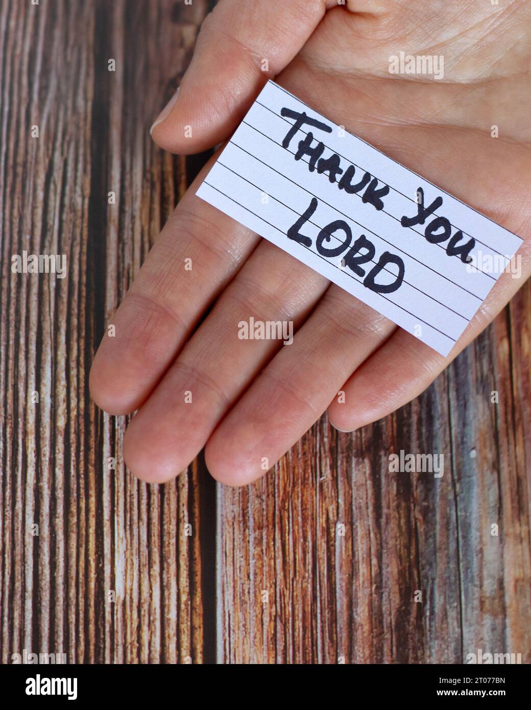 Hand holding note with handwritten text: Thank You LORD over wooden ...