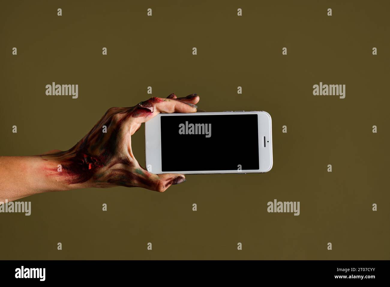 Zombie hand holding mobile phone with blank screen on green background ...