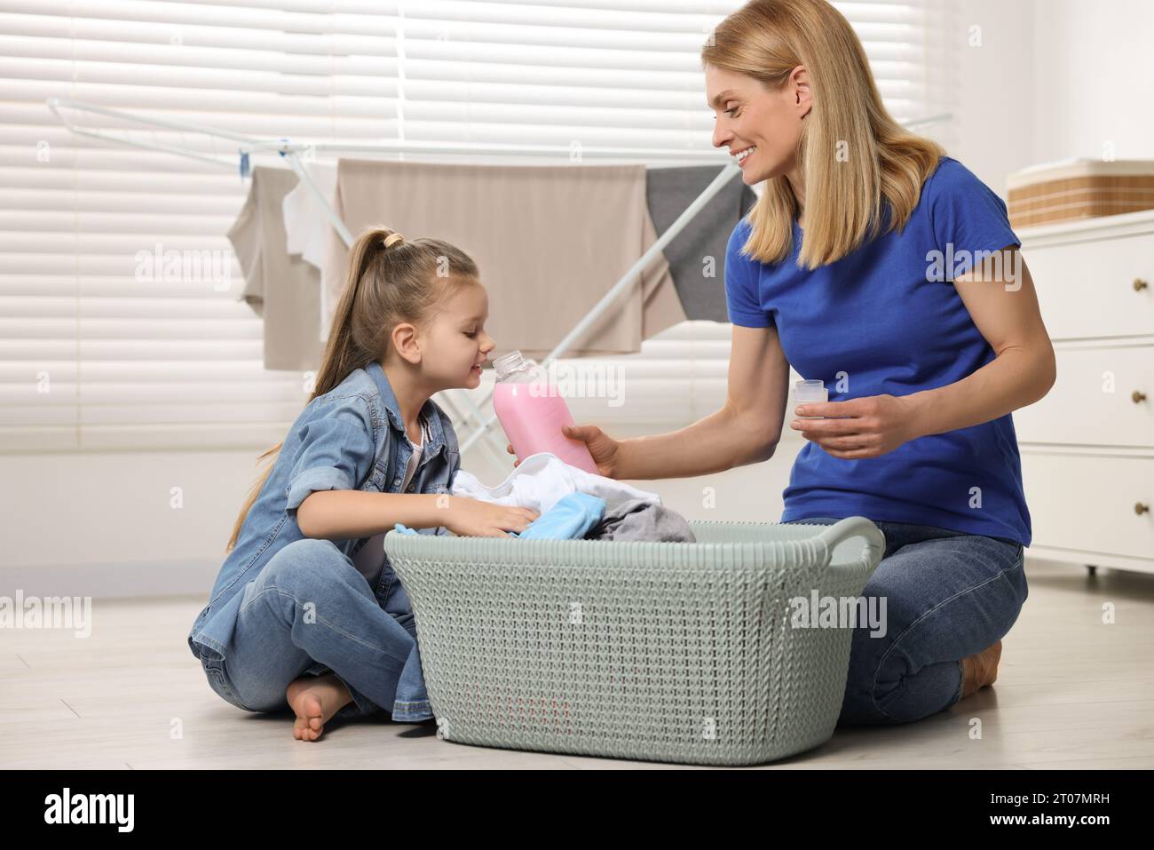 Mother and daughter sitting near basket with dirty clothes and smelling ...