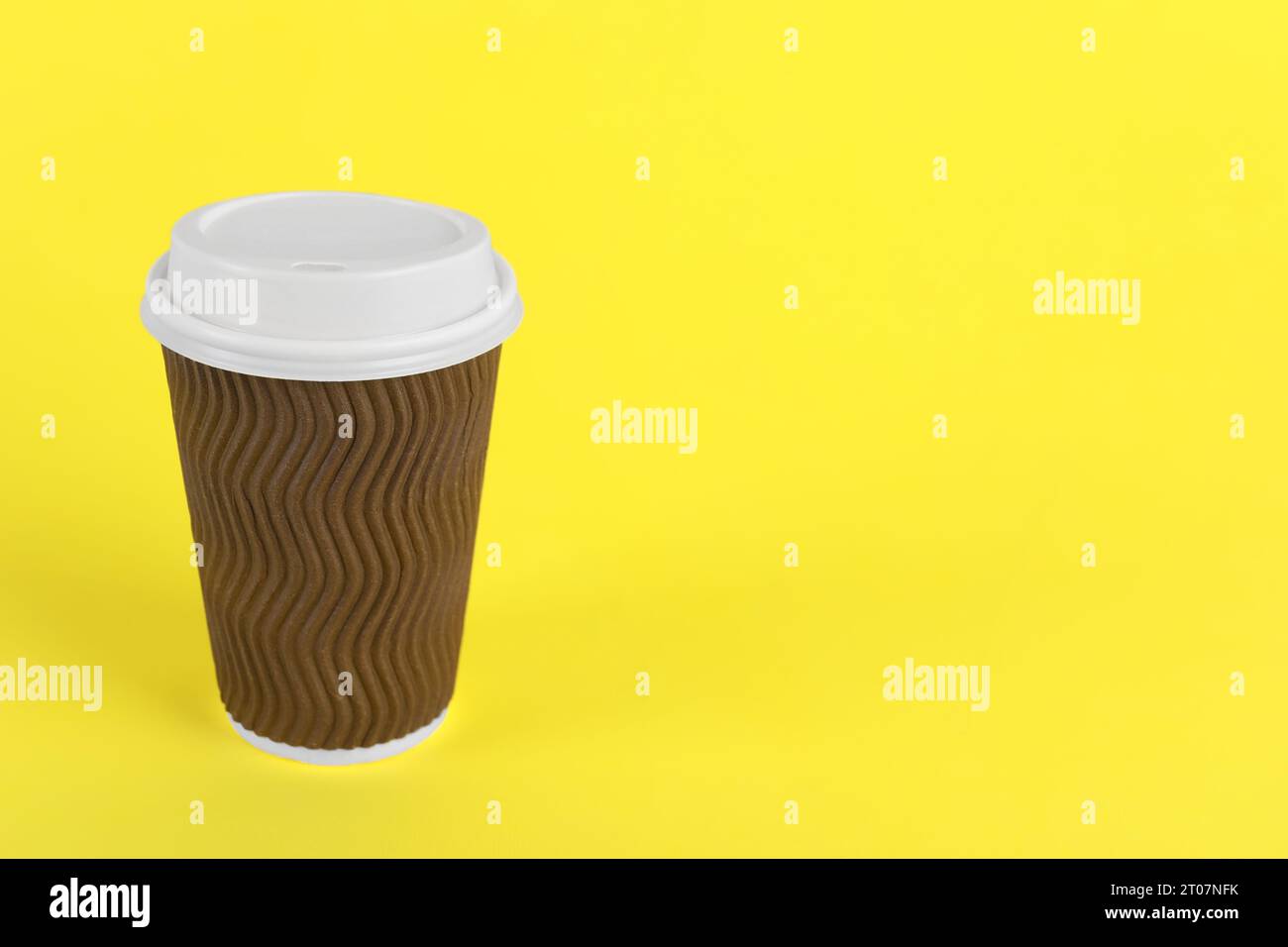 Brown paper cup with plastic lid on yellow background, space for text ...