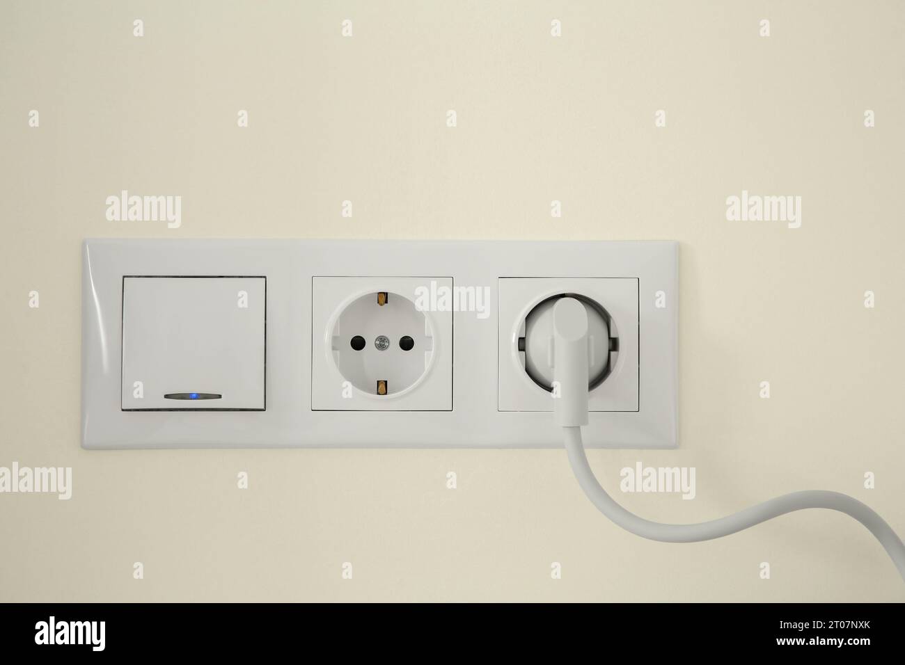 Power sockets with inserted plug and light switch on white wall indoors ...