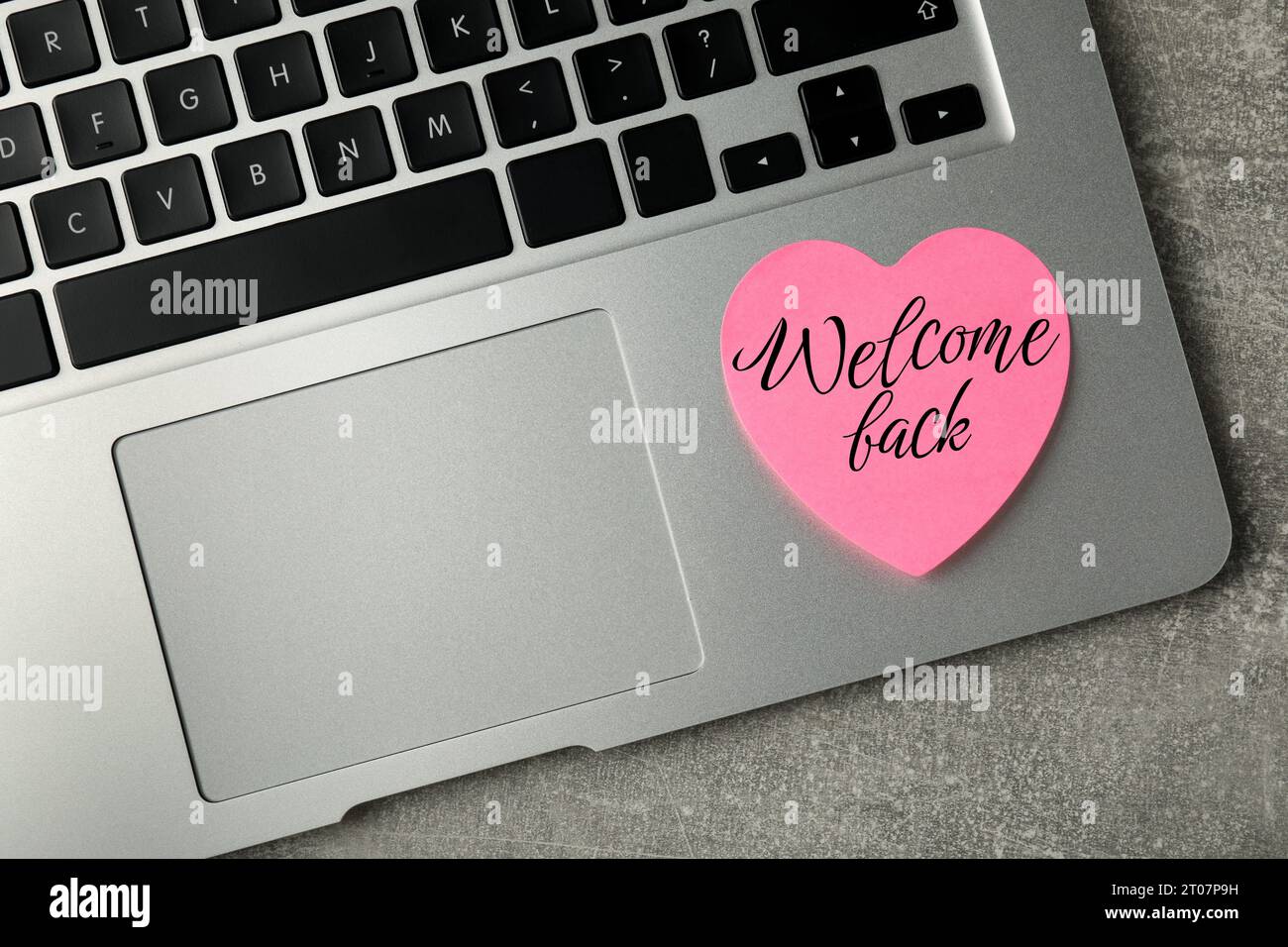 Heart-shaped sticky note with phrase Welcome Back on laptop, top view ...