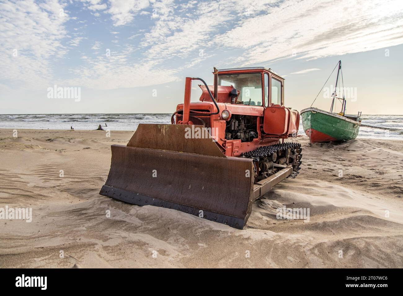 Red Caterpillar Tractor Bulldozer on a beach pulling green wooden boat ...