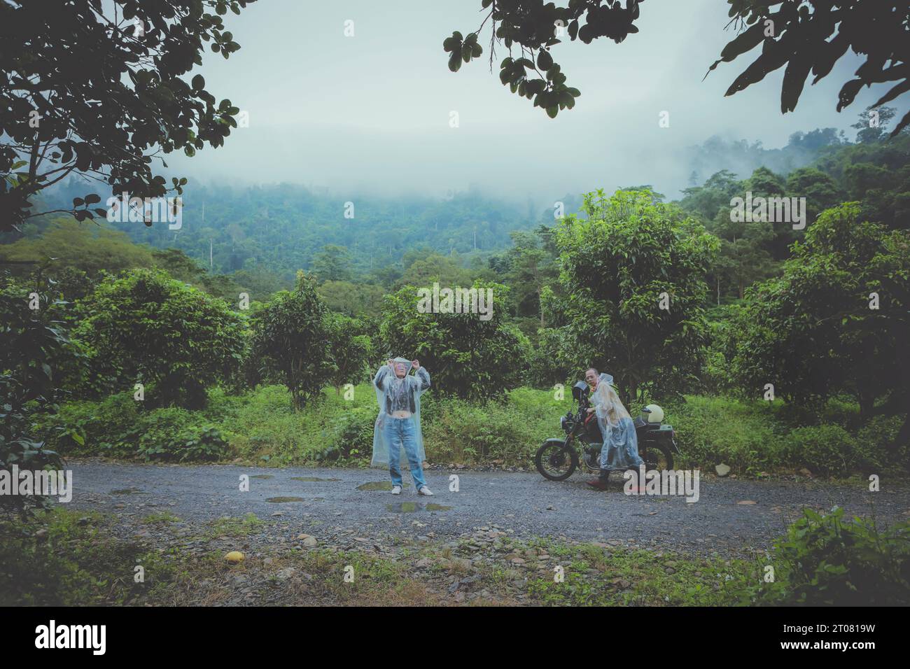 couples of biker pulling small enduro motorcycle on country track among ...