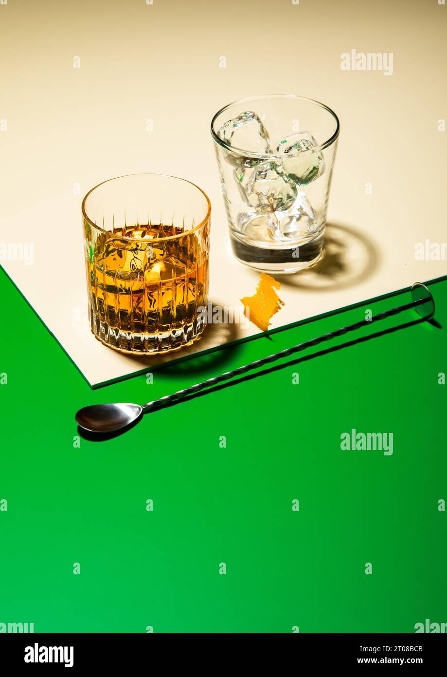 Glass of whiskey with ice and bar spoon with orange peel on green ...